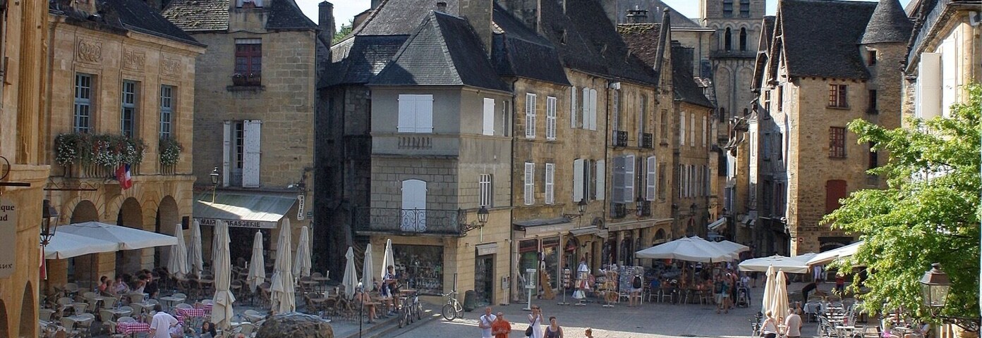 Uma praça histórica com calçamento de pedra, arquitetura europeia tradicional e áreas de estar ao ar livre.