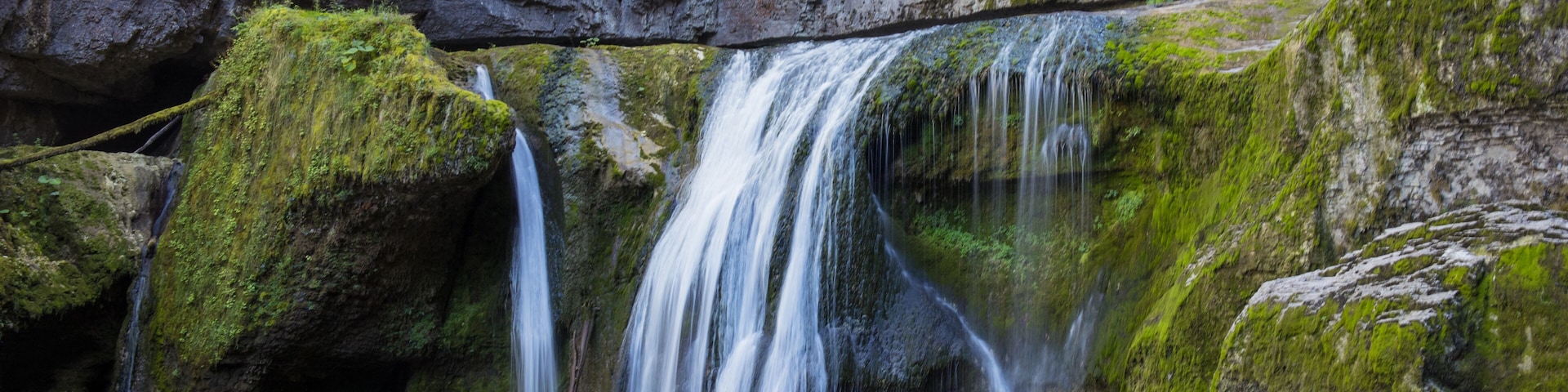 Uma cascata em vários níveis deságua sobre rochas cobertas de musgo em uma piscina cristalina.