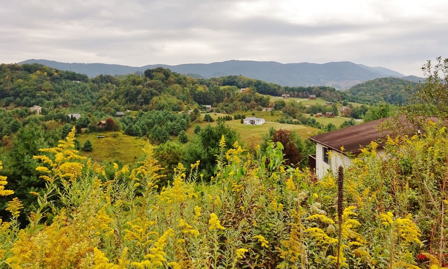 Paisagem rural com colinas onduladas, casas dispersas e vegetação densa.