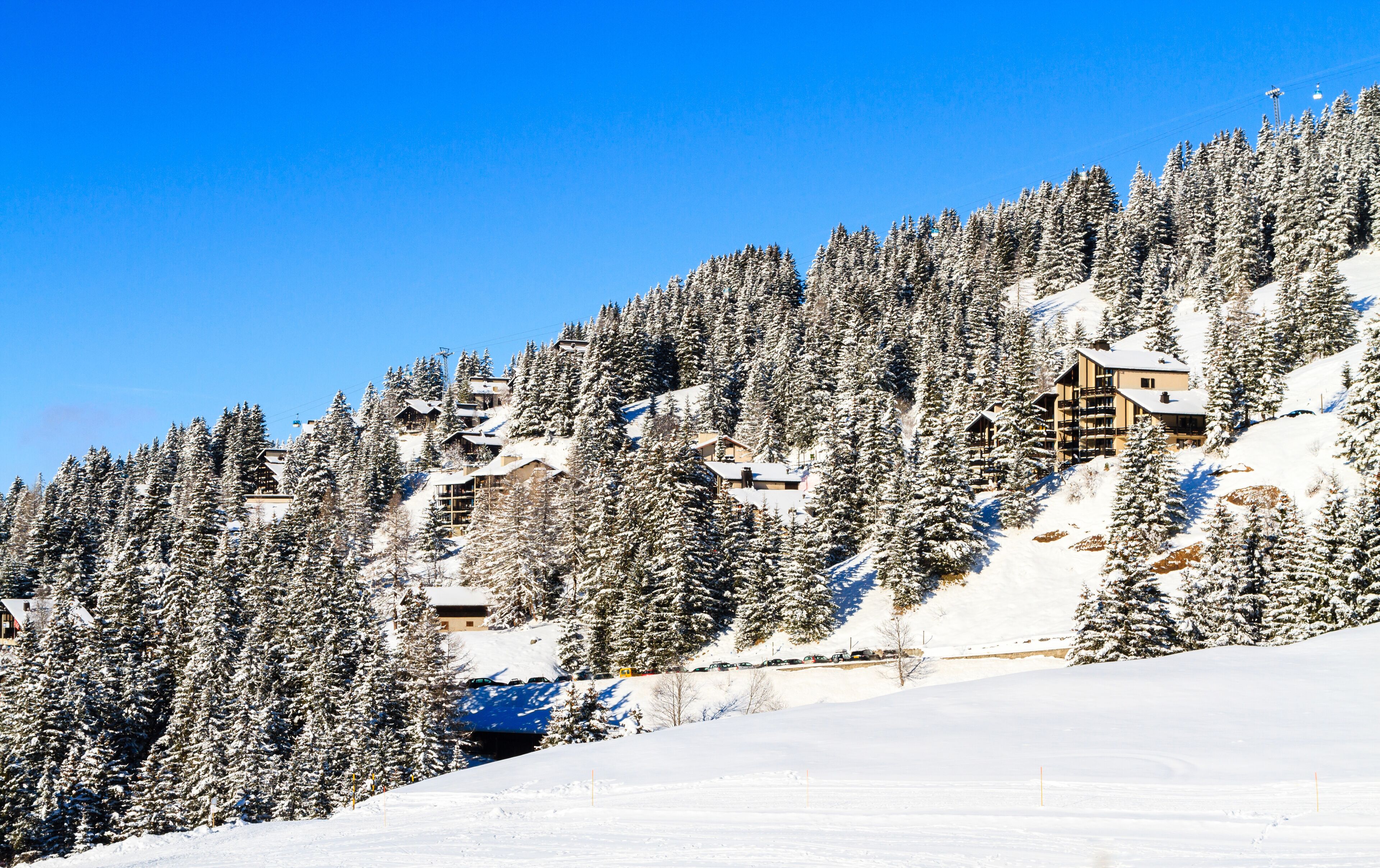 Montanha coberta de neve com chalés de esqui e céu azul límpido.