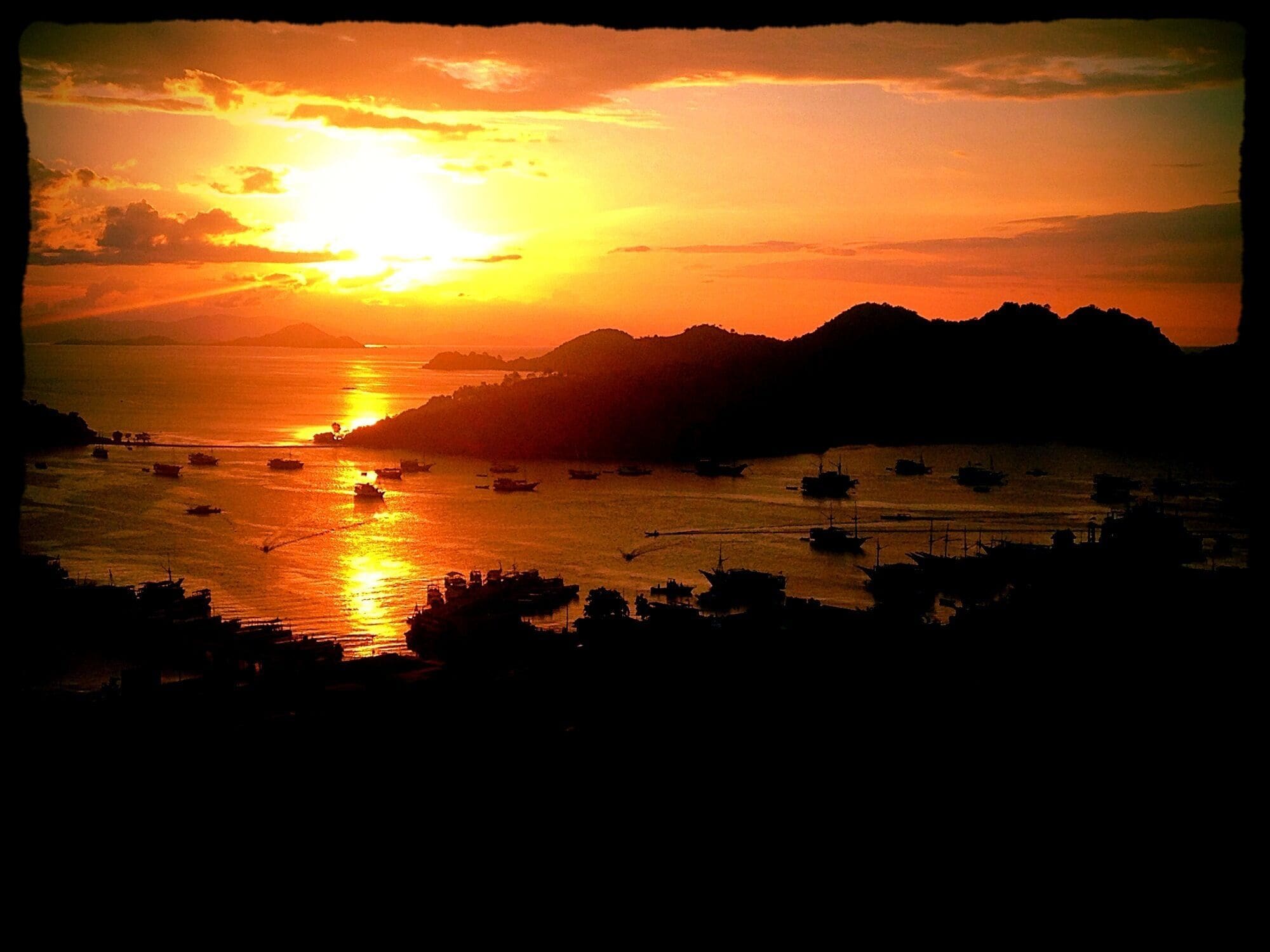 Um pôr do sol sobre uma área costeira com barcos e uma paisagem montanhosa.