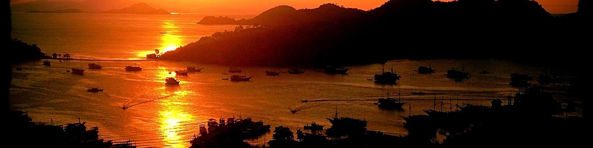 Um pôr do sol sobre uma área costeira com barcos e uma paisagem montanhosa.