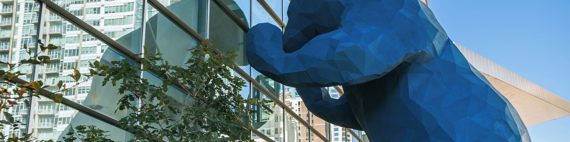 Uma escultura de urso azul em frente a um edifício moderno de vidro.