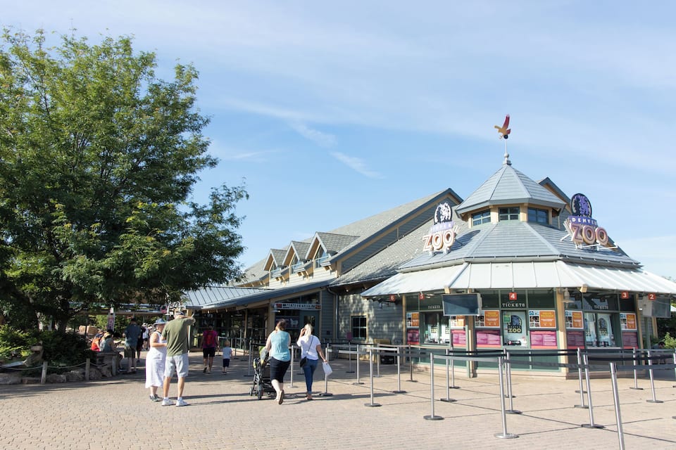 Um jardim zoológico com bilheteiras e uma grande árvore em primeiro plano.