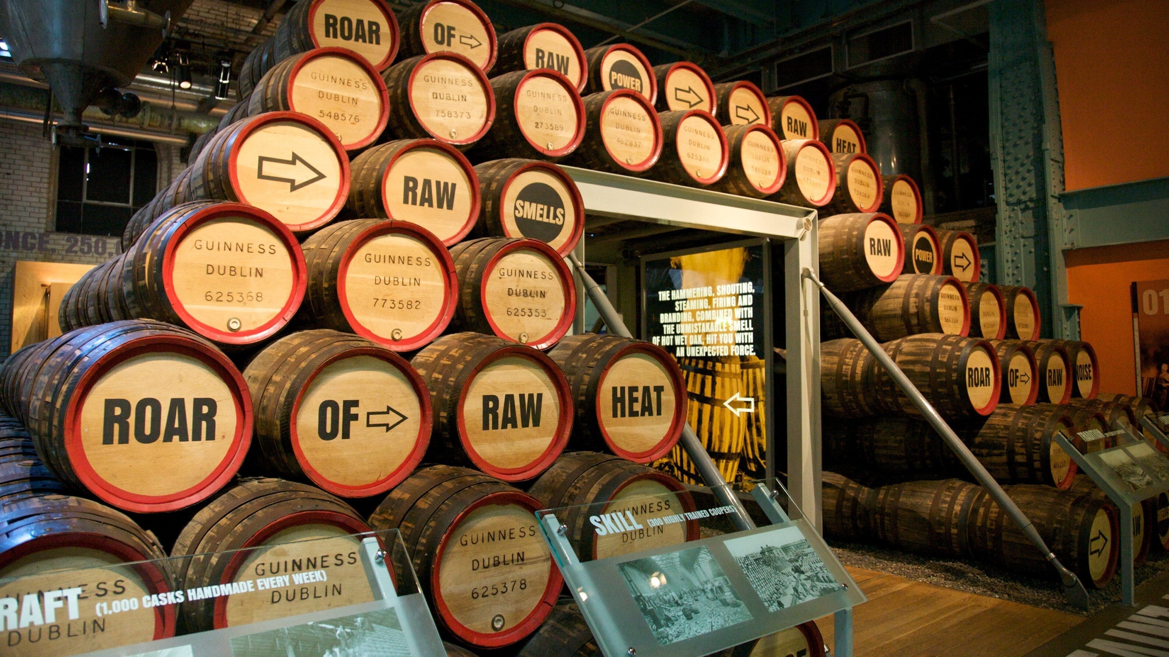 Pilhas de barris de cerveja Guinness com etiquetas indicando sabores como 'Roar', 'Raw' e 'Heat'.