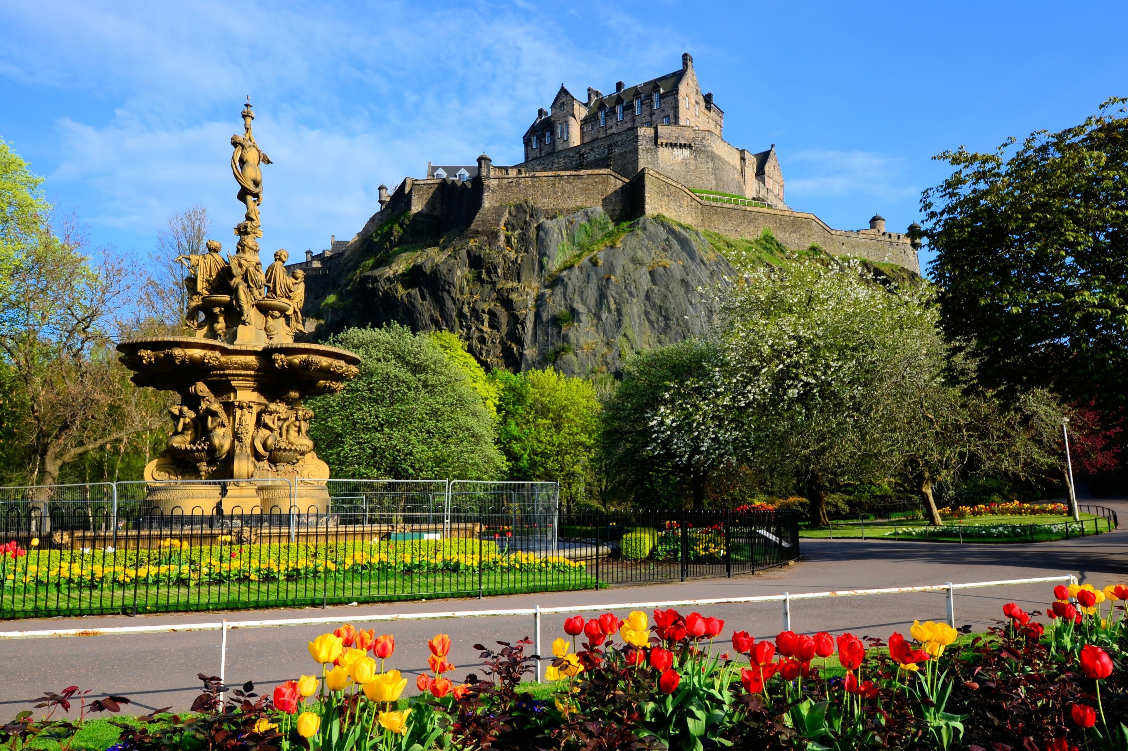 Um castelo numa colina, uma fonte e tulipas num parque.