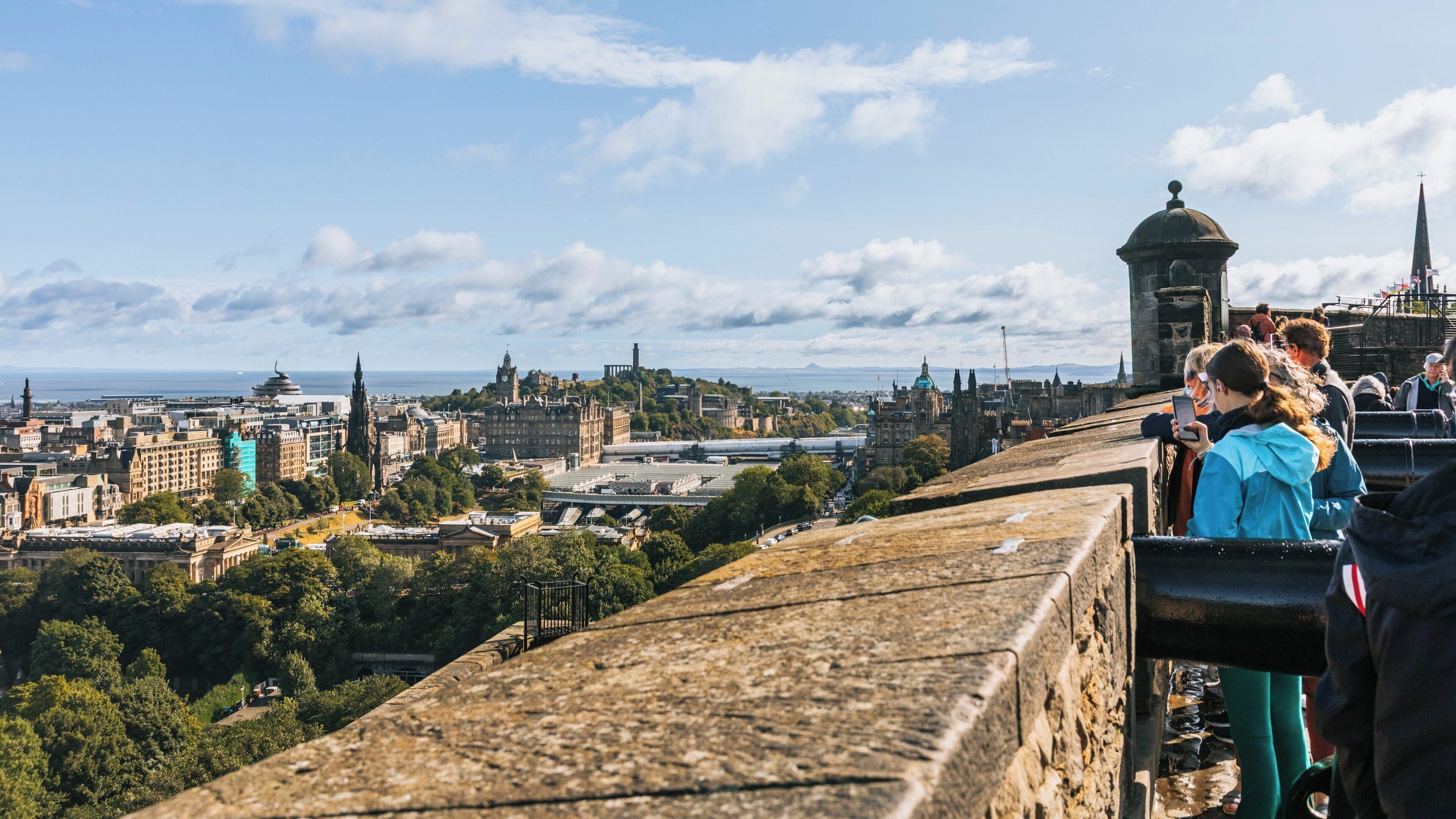 Visitors enjoying panoramic views from Edinburgh Castle in Old Town, Scotland, observing the cityscape and surrounding landscape on a clear day