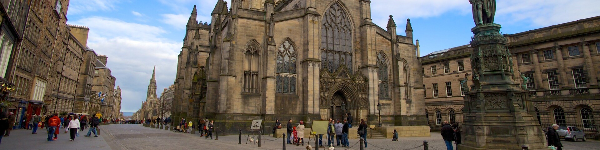 Uma catedral histórica com arquitetura gótica detalhada, uma estátua e uma praça de paralelepípedos.