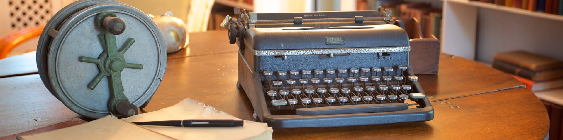 Uma máquina de escrever antiga sobre uma mesa de madeira, com um caderno e uma caneta ao lado.