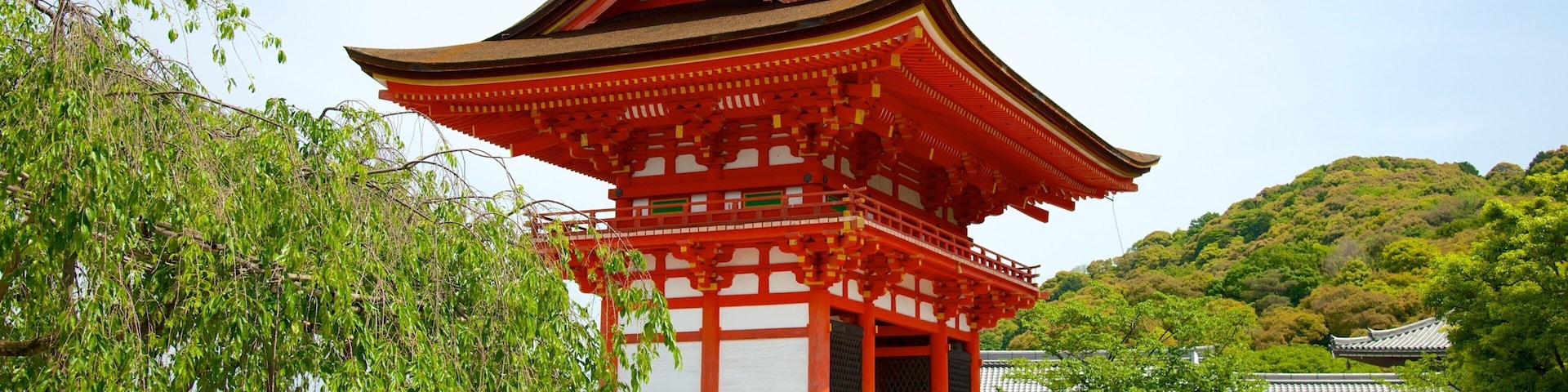 Um pagode japonês tradicional com esquema de cores vermelho e branco, cercado por vegetação exuberante e um céu claro.