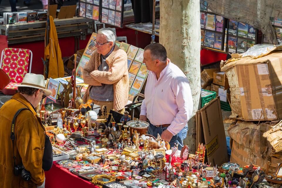 Um mercado ao ar livre movimentado com diversos quiosques vendendo antiguidades e objetos de coleção.