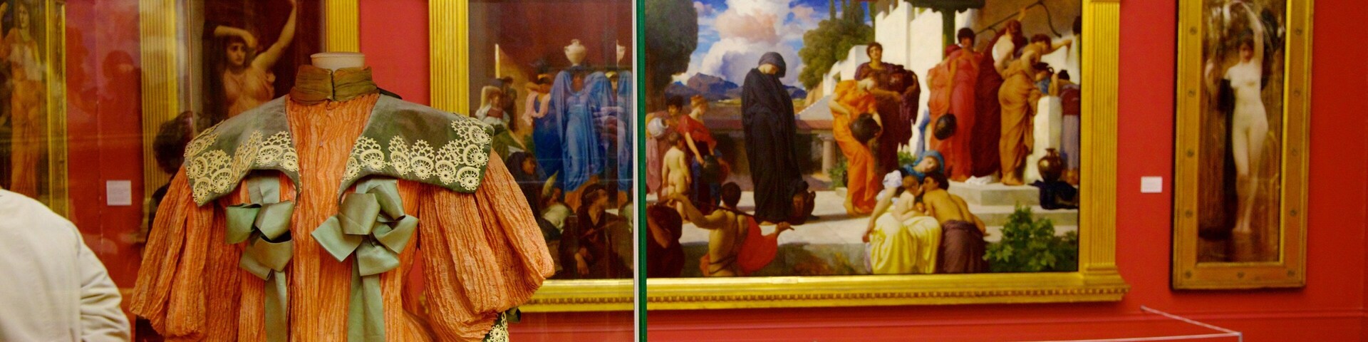 Uma exposição de museu com um manequim vestido com traje típico e duas grandes pinturas nas paredes.