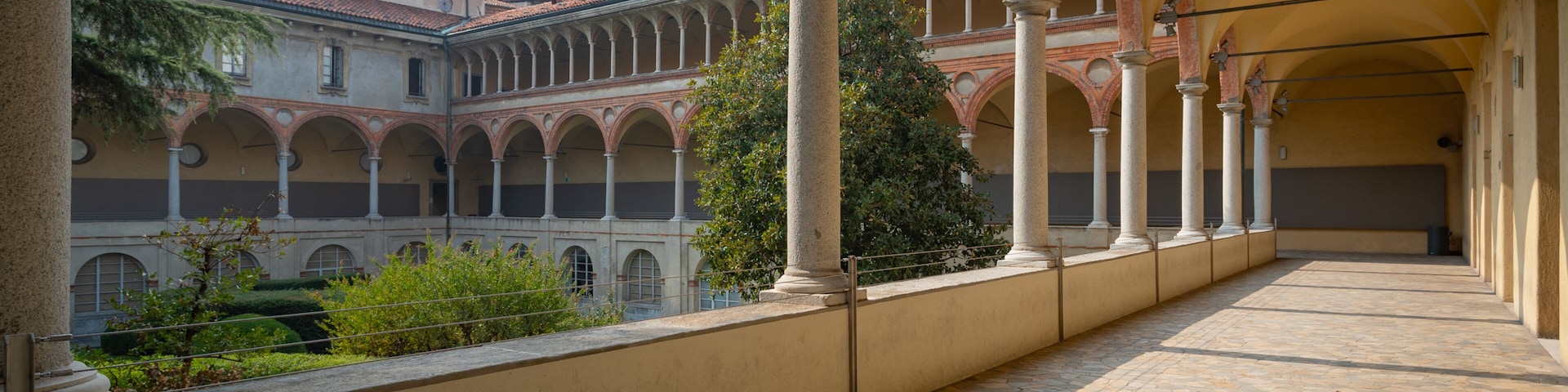 Um pátio com piso de azulejos, colunas e um edifício com cúpula e campanário ao fundo.