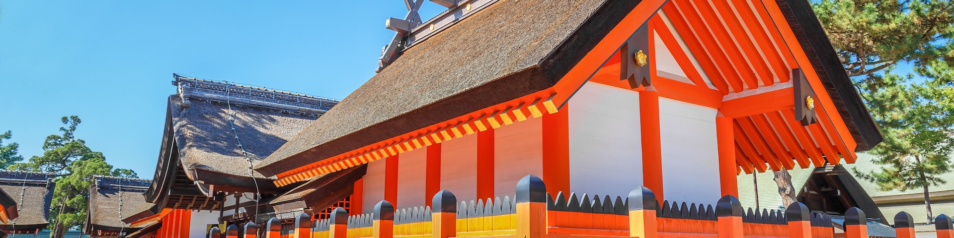 Um edifício japonês tradicional com paredes laranja vibrantes e brancas, um telhado de palha e uma cerca com design de piquete.