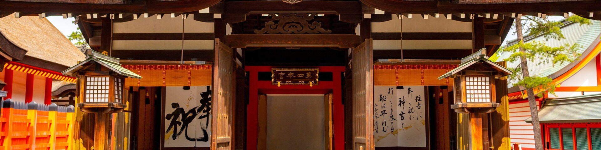Um templo japonês tradicional com telhado de palha, vigas de madeira e um portão de entrada vermelho.