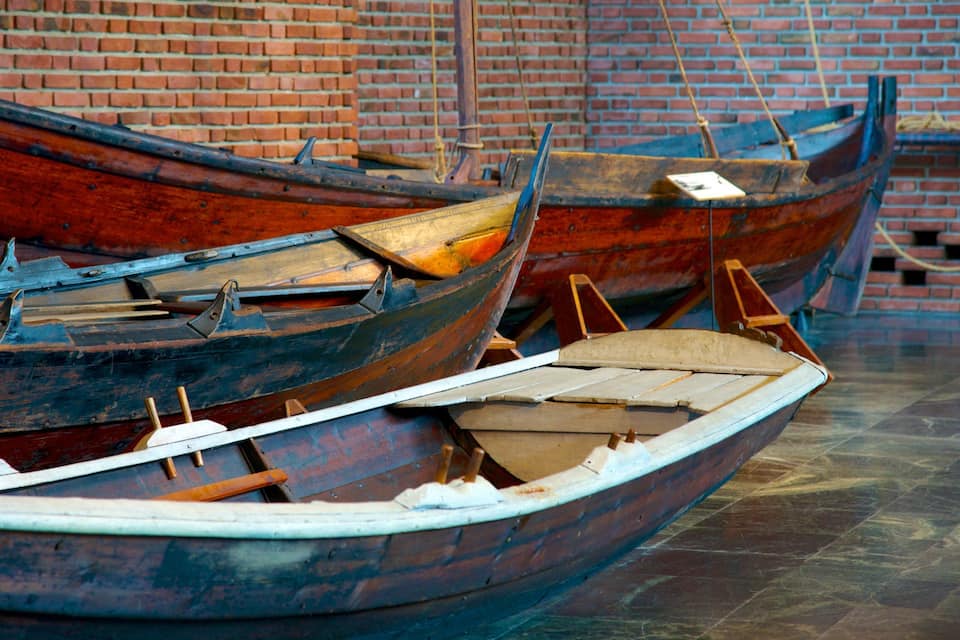 Vários barcos de madeira com detalhes metálicos, exibidos em frente a um muro de tijolos.