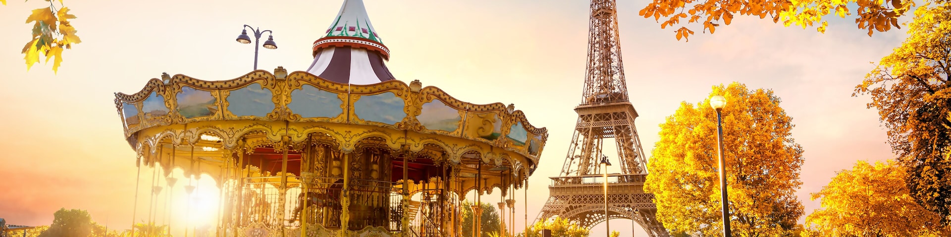 Um carrossel com topo pontiagudo, a Torre Eiffel e árvores de folhagem outonal.