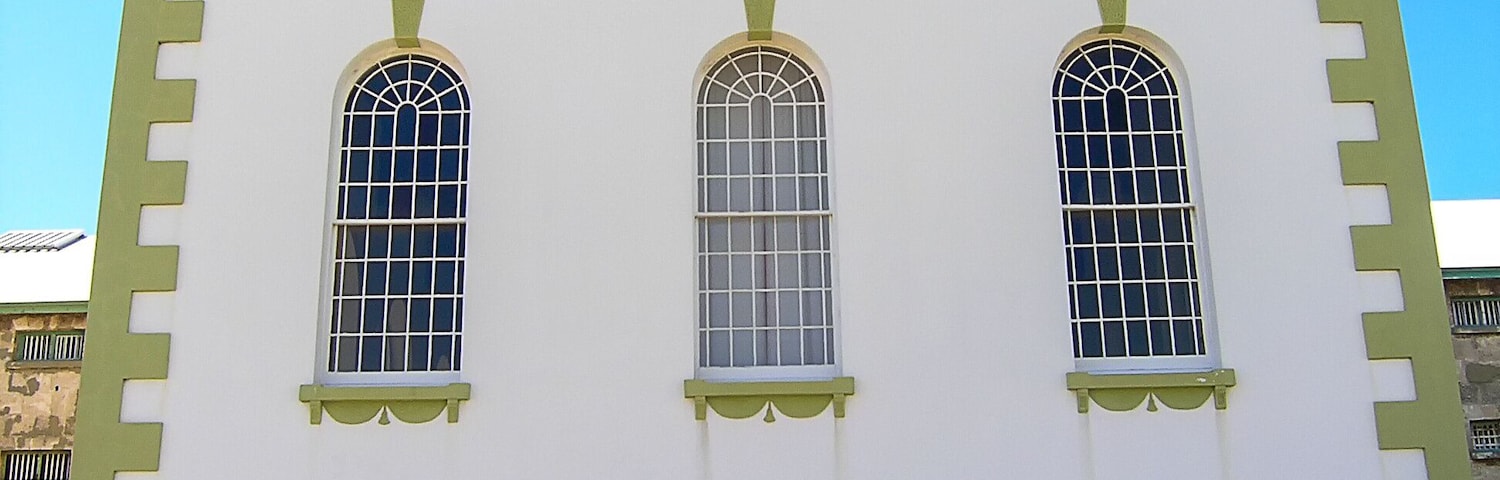 Um edifício branco com detalhes verdes e três janelas em arco, identificado com 'VR 1855' e um símbolo de coroa.