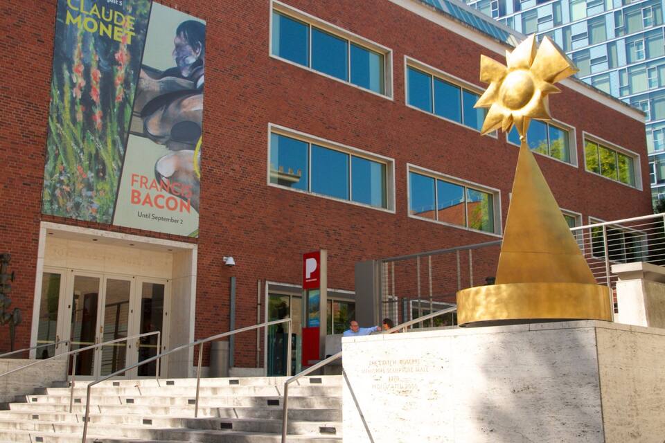 Um edifício com um grande anúncio de Francis Bacon, uma escadaria pública e uma escultura dourada.