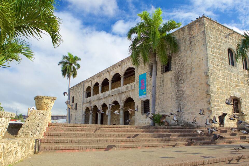 Um edifício histórico de pedra com arcos e palmeiras.