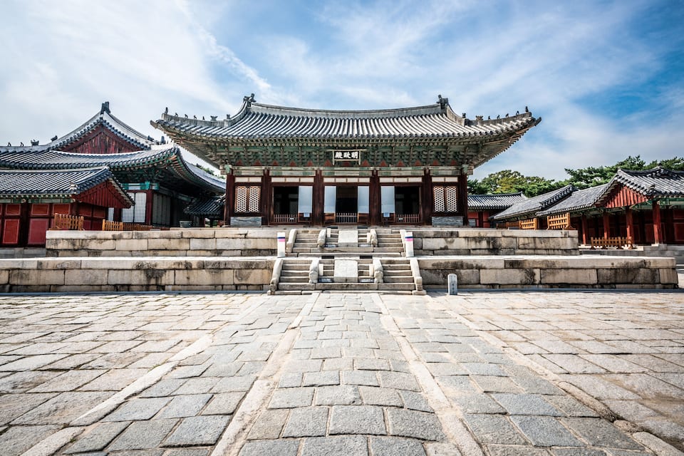 Um palácio coreano tradicional com um portão grande e ricamente decorado e degraus de pedra que levam até ele.