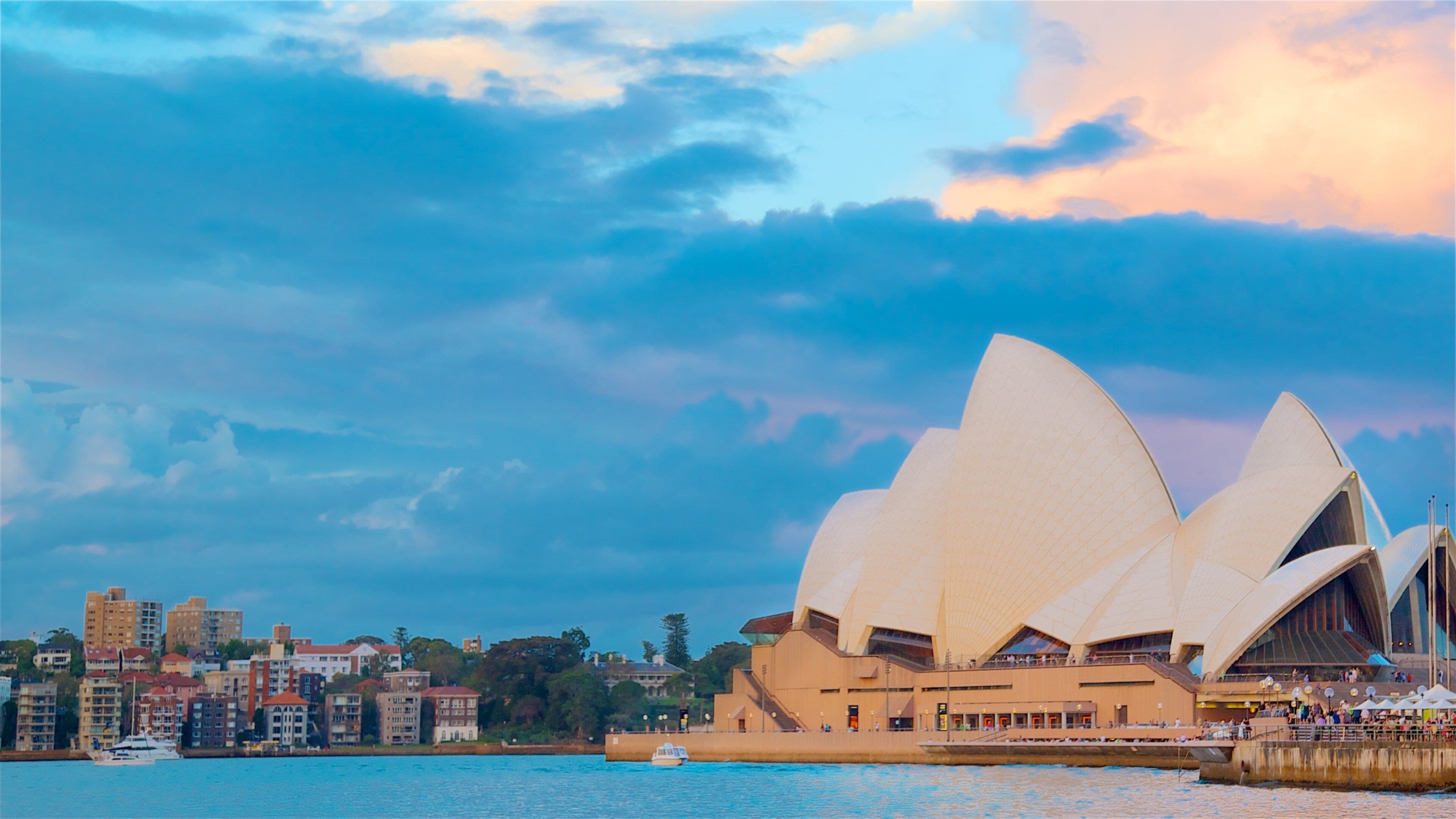 A Ópera de Sydney, com seu design branco e distinto semelhante a velas, com o céu azul e nublado ao fundo.