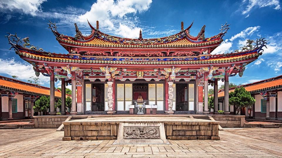 Um templo tradicional chinês com arquitetura ornamentada, um pátio de pedra e um céu azul límpido.