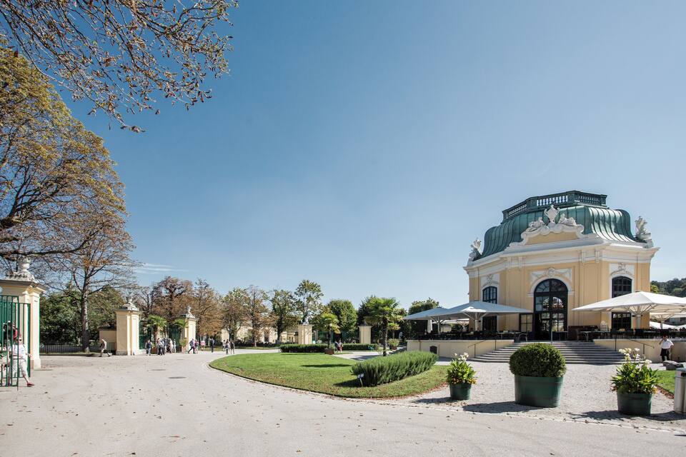 Um edifício grande e ornamentado com uma cúpula verde, rodeado por um jardim bem cuidado e áreas de estar ao ar livre.