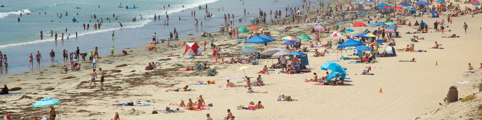 Praia cheia de gente se banhando e tomando sol.