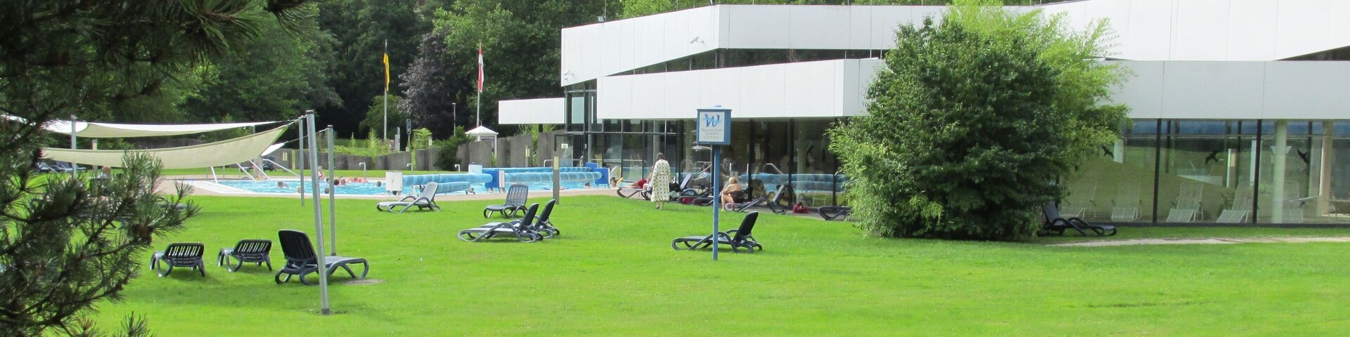 Um edifício moderno com piscina e espreguiçadeiras num relvado.
