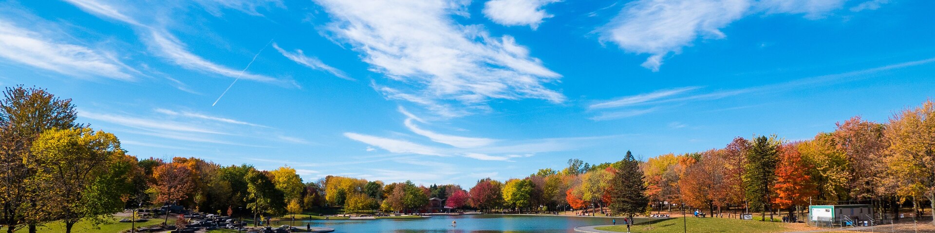 Um parque com um lago grande, árvores com cores de outono e um céu azul límpido.