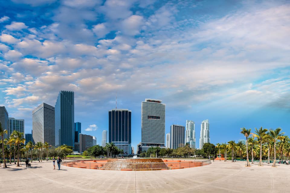 Paisagem urbana com edifícios altos, palmeiras e uma orla marítima.