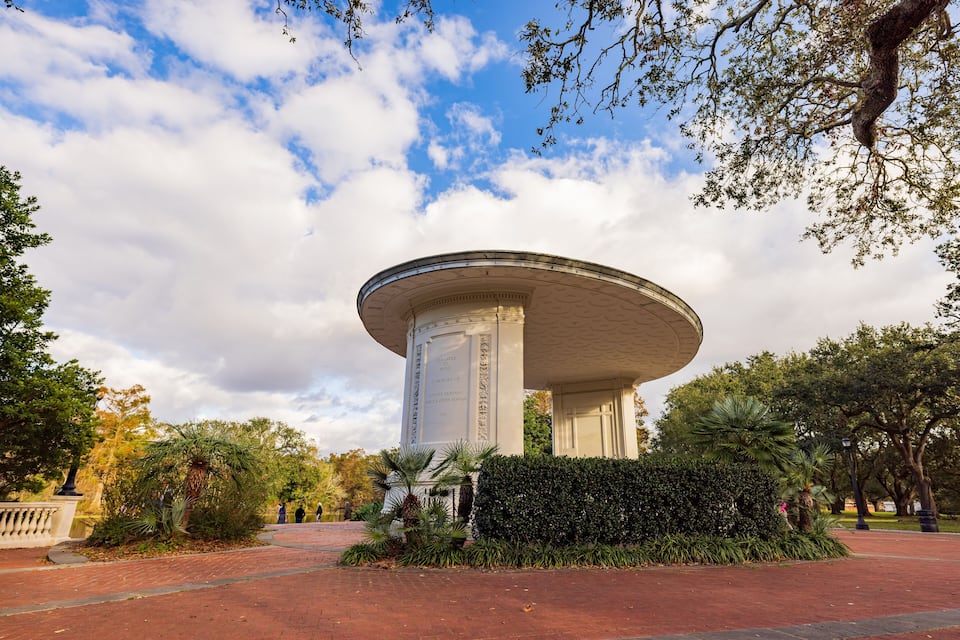 Um grande monumento circular rodeado por vegetação e um caminho de tijolos.