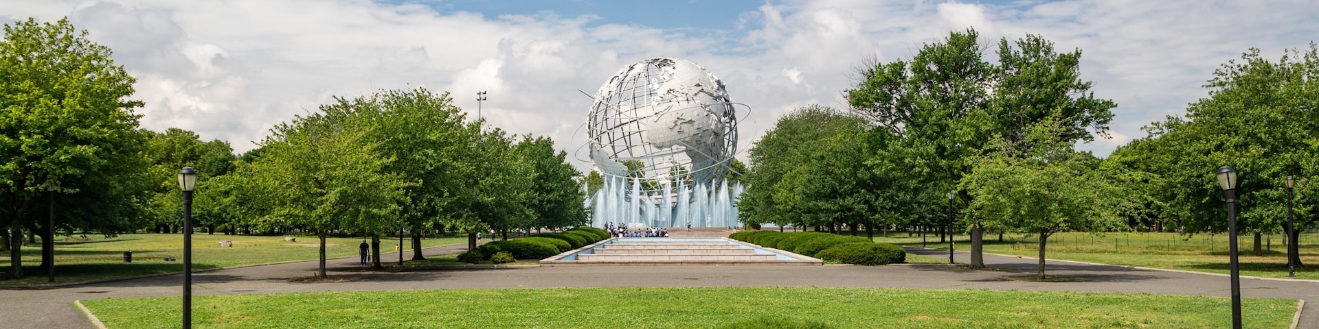 Escultura de um globo em um parque com árvores verdes e céu claro.