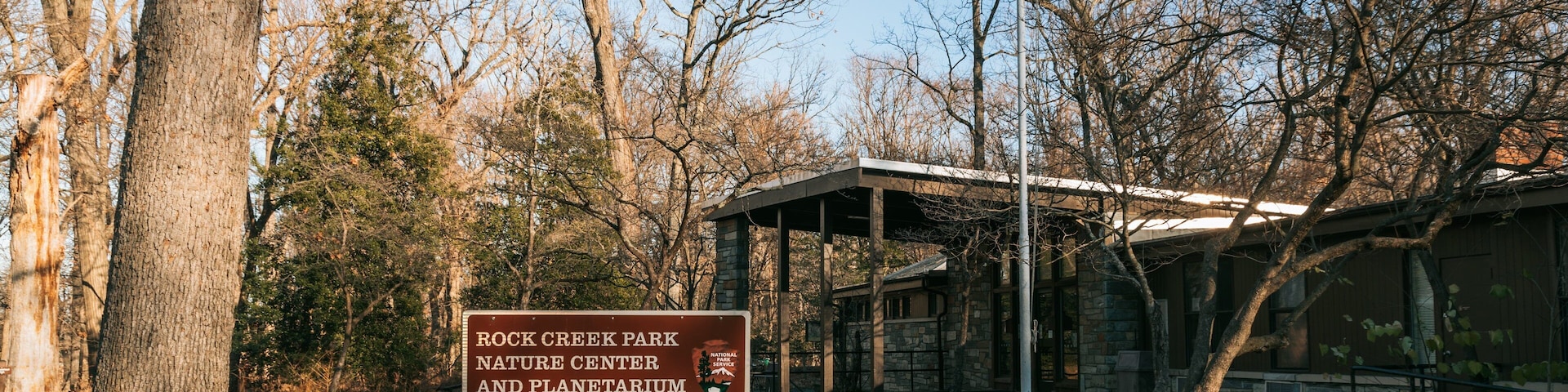 Placa para o Centro de Natureza e Planetário do Parque Rock Creek, com uma bandeira americana ao fundo.