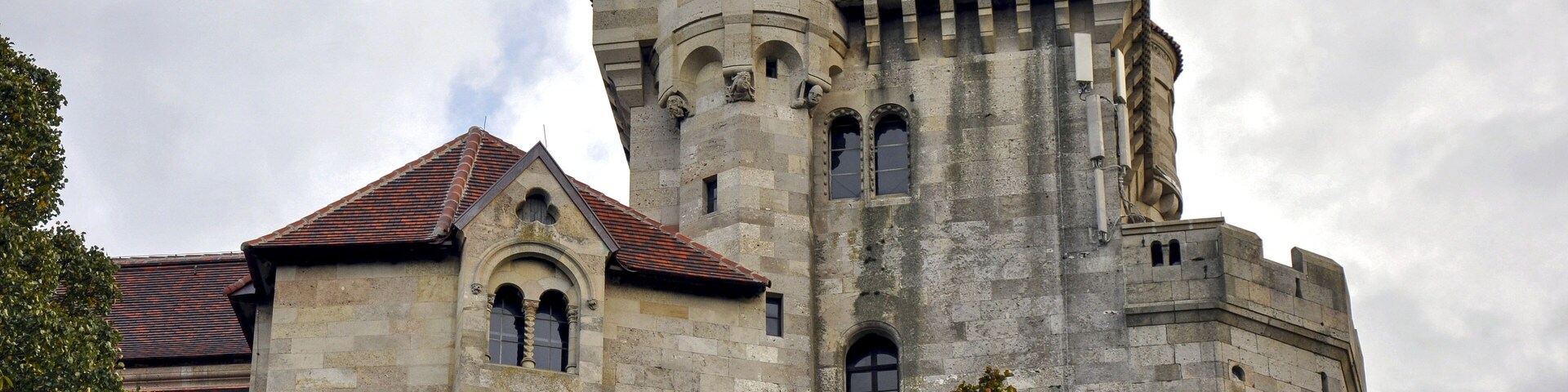Um castelo de pedra histórico com telhado de telhas vermelhas e janelas em arco.