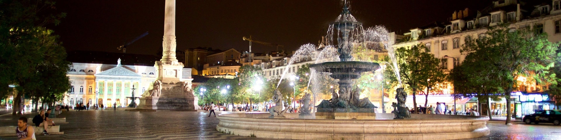 Uma praça com uma fonte, um monumento e piso estampado.