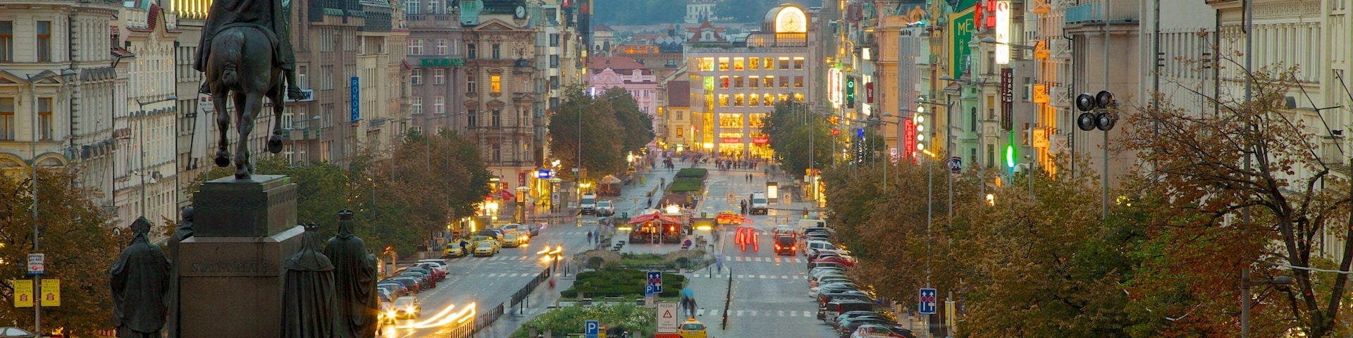 Rua movimentada no centro da cidade, com edifícios históricos e uma estátua.