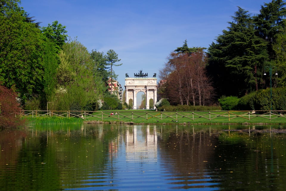 Um parque com um grande arco, um lago e árvores ao redor.
