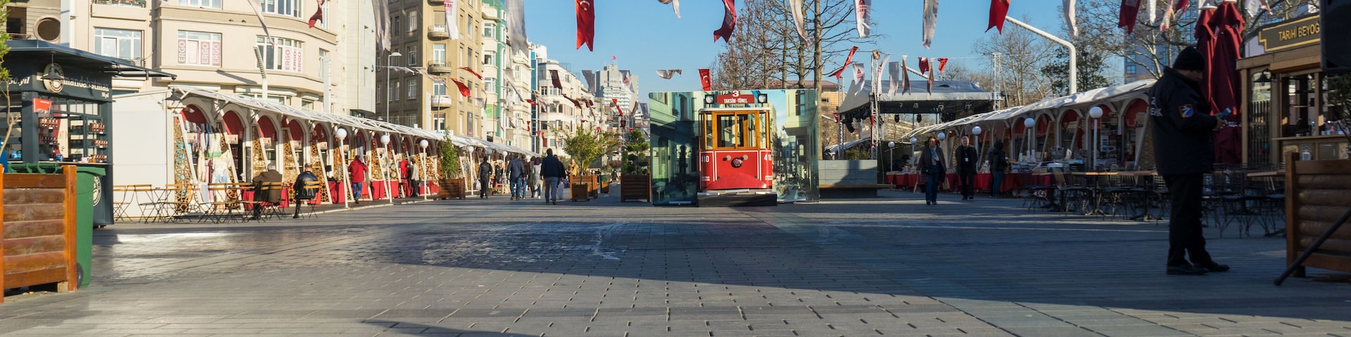 Um elétrico numa praça urbana, com edifícios e bandeiras.