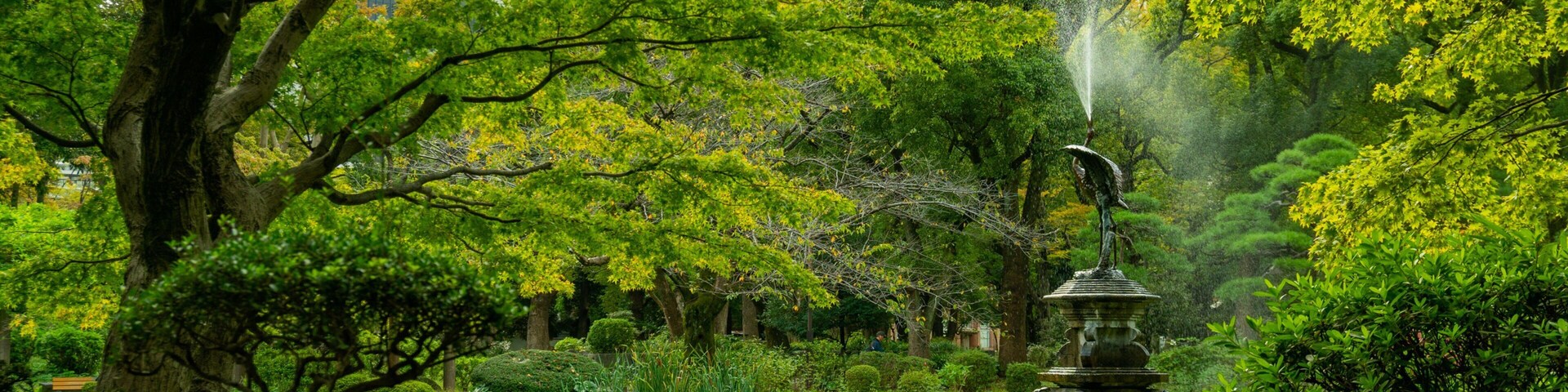 Um jardim tranquilo com lago, vegetação exuberante e uma estátua de fonte.