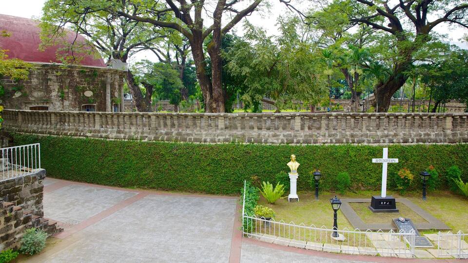 Um muro de pedra histórico, uma estátua e uma placa em um parque.