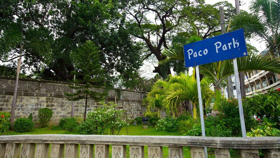 Placa com a inscrição 'Paco Park', com vegetação exuberante e um muro de pedra ao fundo.