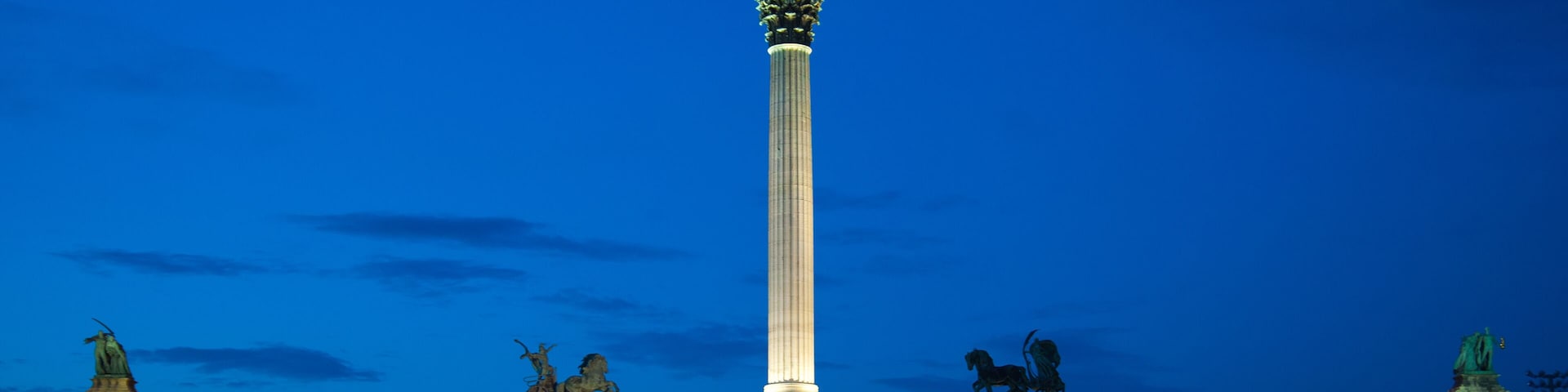 Um grande monumento com colunas e estátuas na base, rodeado por uma praça pavimentada.