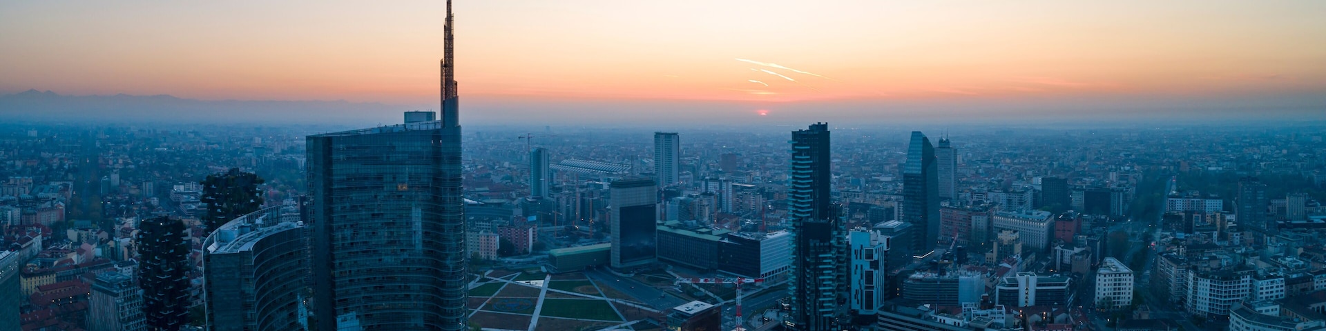 Paisagem urbana com arranha-céus imponentes e um pôr do sol ao fundo.