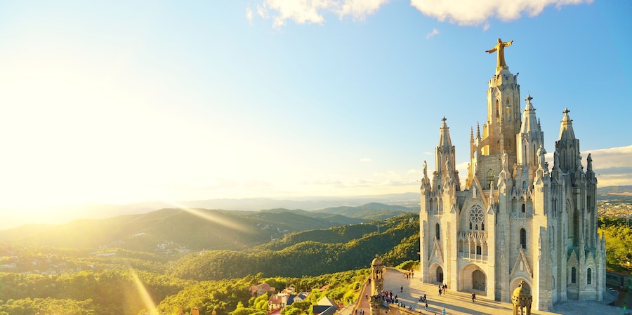 Uma catedral com múltiplas torres, rodeada por colinas verdejantes e um céu límpido.