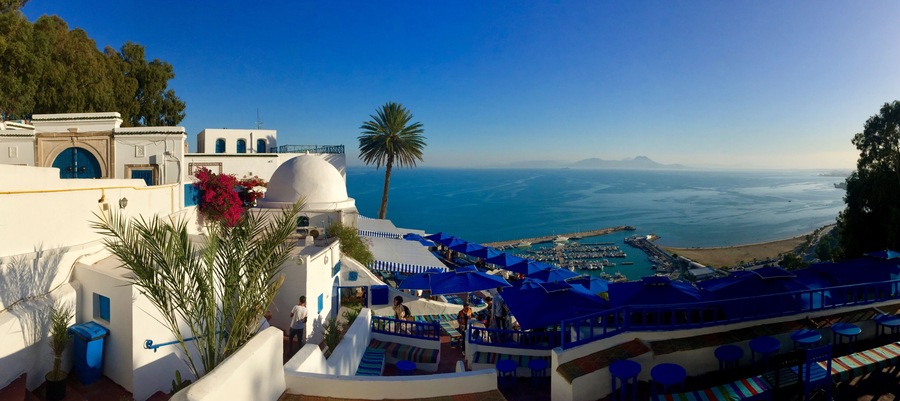 Um resort costeiro com edifícios brancos, guarda-sóis azuis e vista para o mar.