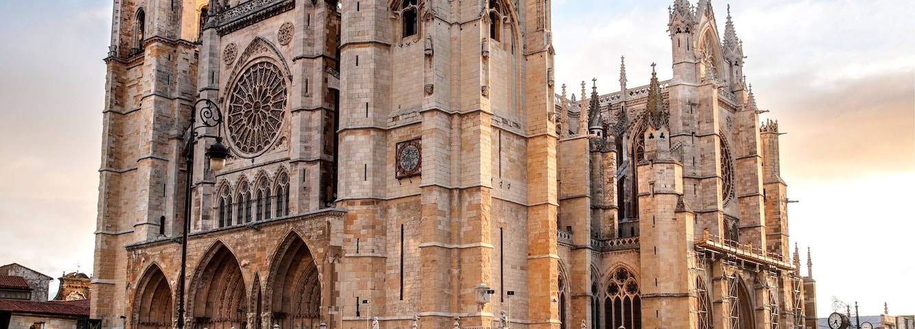 Uma catedral grande com arquitetura gótica elaborada, uma rosácea destacada e um reflexo no chão molhado.
