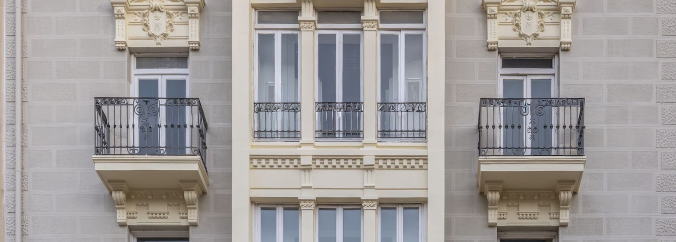 Um edifício de vários andares com detalhes arquitetônicos ornamentados, incluindo varandas decorativas e um frontão central.