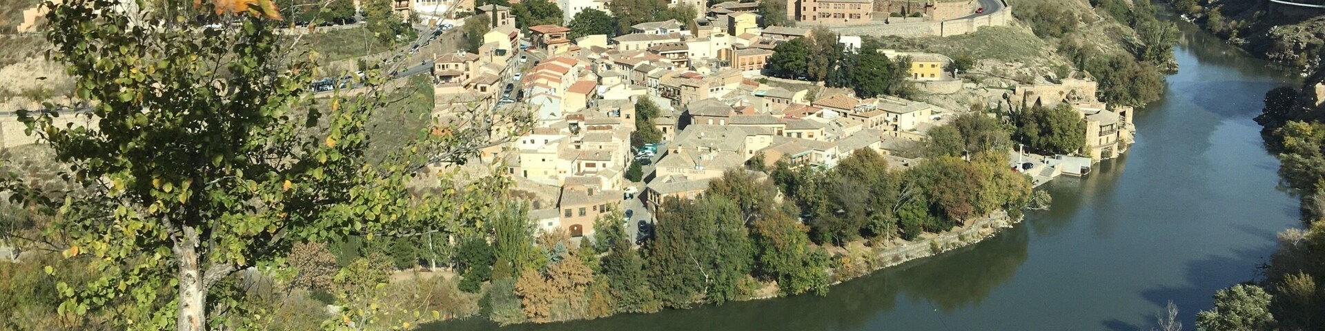 Um rio serpenteia por uma cidade densamente construída, com uma imponente estrutura semelhante a um castelo ao fundo.